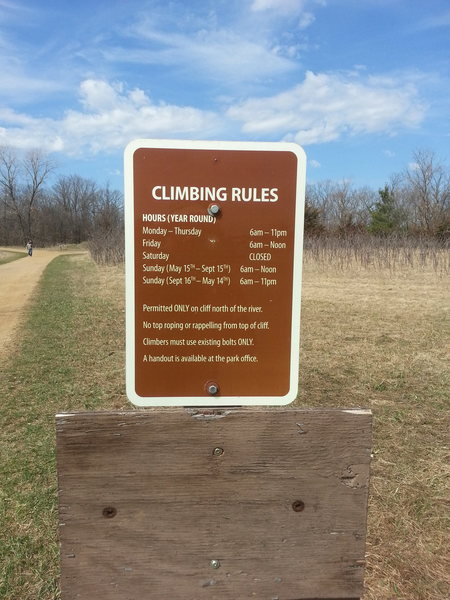 New park climbing rules and hours open sign at climbers parking lot.
